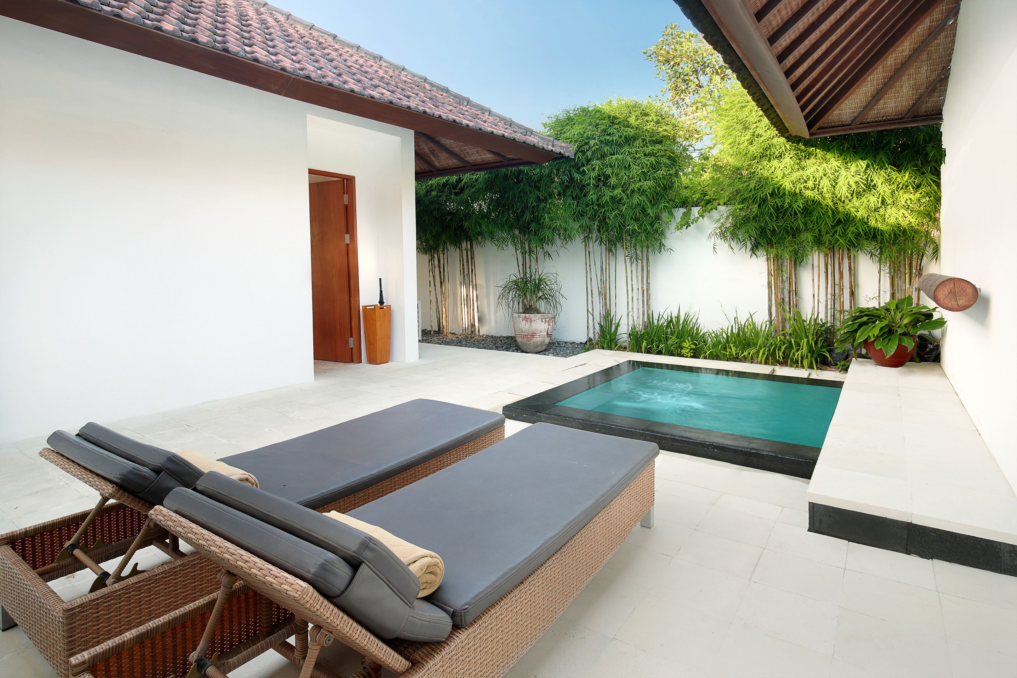 Área de piscina com duas espreguiçadeiras, uma piscina pequena e um painel de bambu.