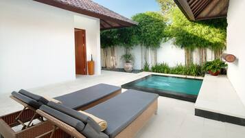 Área de piscina com duas espreguiçadeiras, uma piscina pequena e um painel de bambu.
