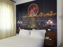 Quarto de hotel com cama, mesa de cabeceira, telefone fixado na parede e um grande mural de roda gigante à noite.
