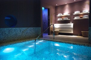 Piscina com azulejos de mosaico, guarda-corpo de metal e prateleiras com toalhas.