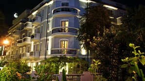 Um hotel com vários andares, varandas, fachada bem iluminada e vegetação exuberante em primeiro plano.