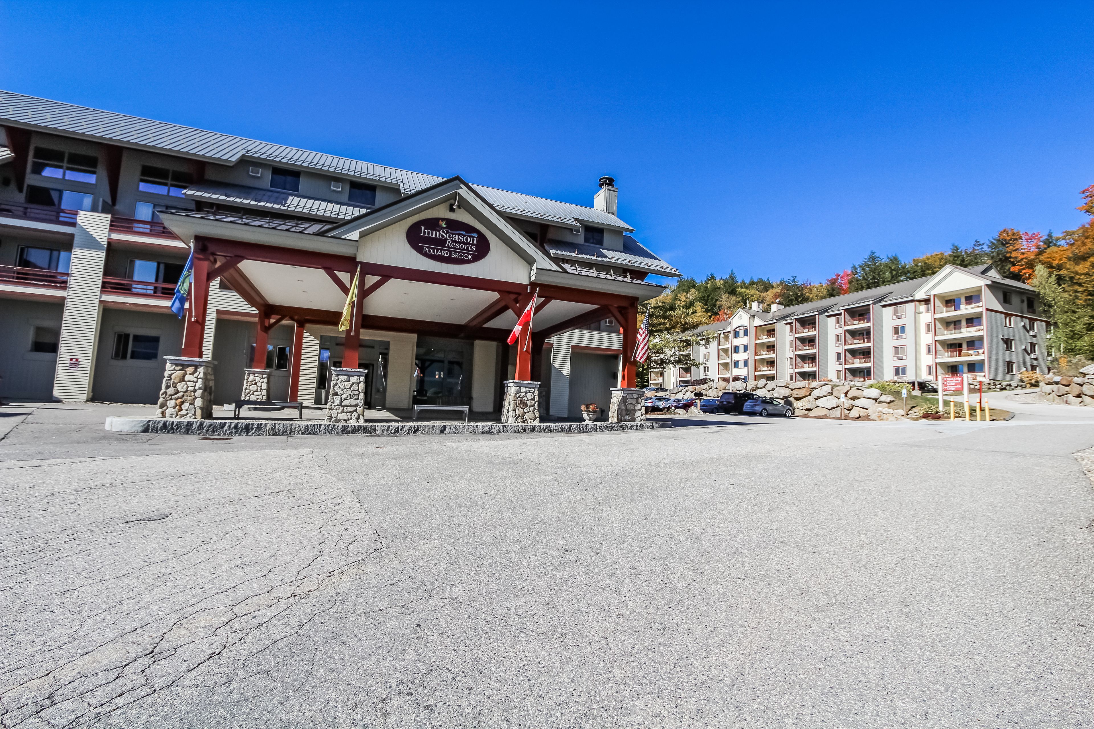Entrada de hotel com varanda coberta, pilares de pedra e uma placa indicando 
