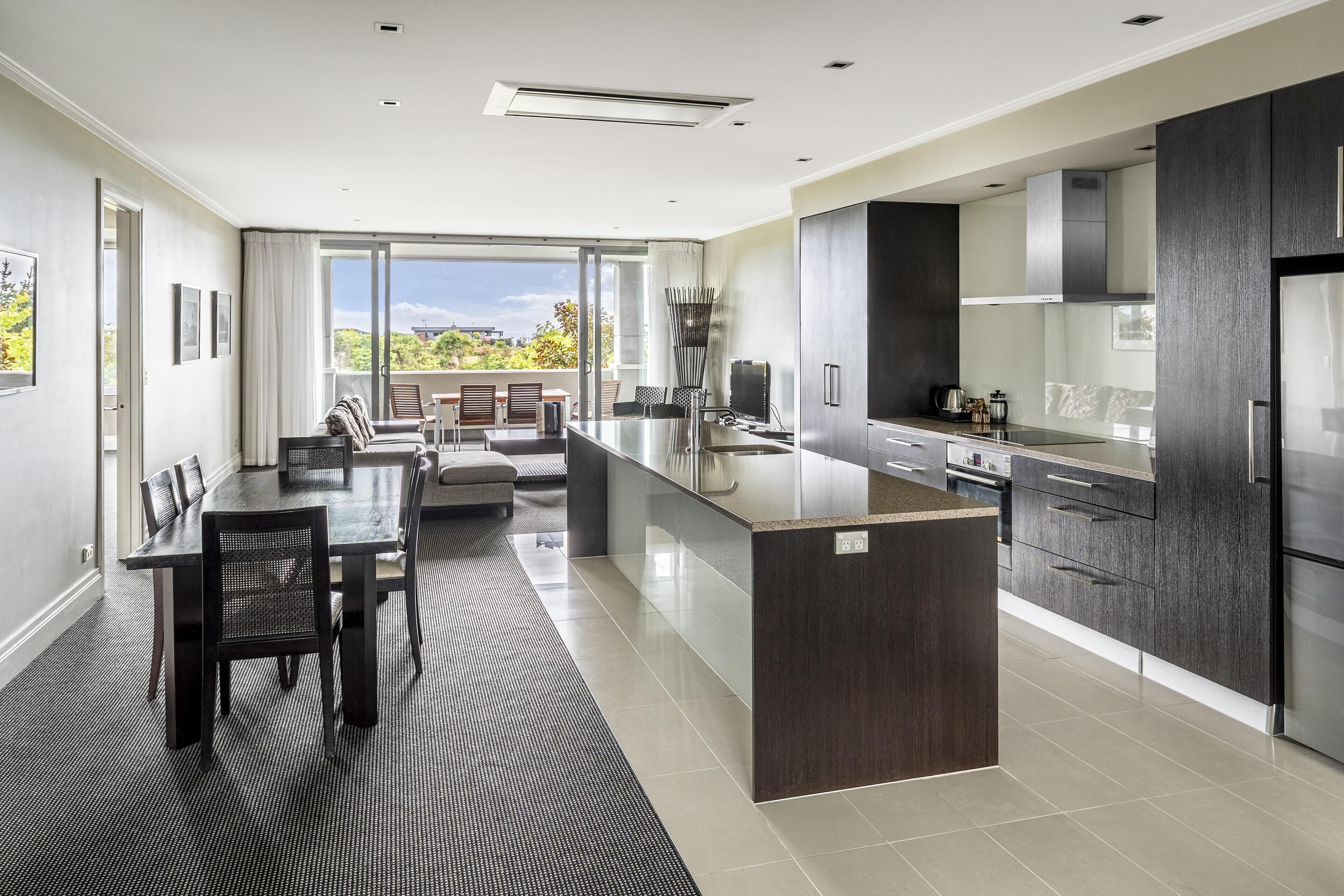 Cozinha moderna com ilha central, armários escuros e área de jantar com vista.