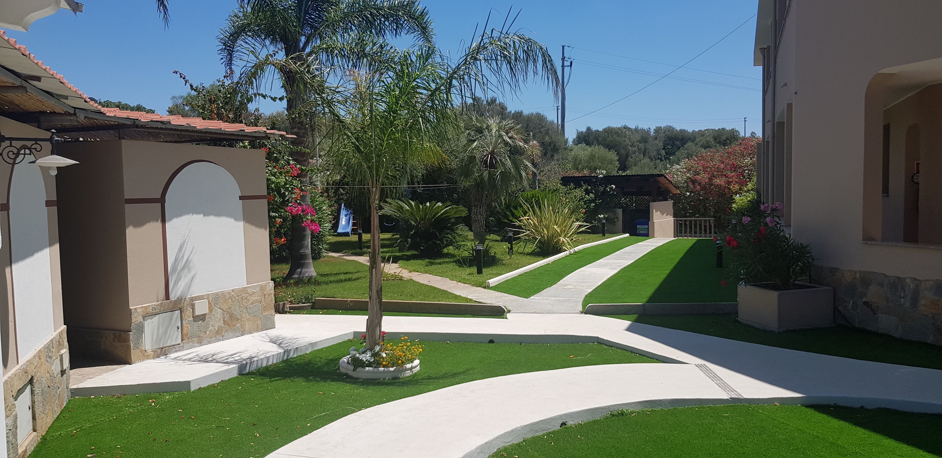 Um jardim bem cuidado com um caminho que leva a um edifício, cercado por vegetação exuberante e plantas floridas.