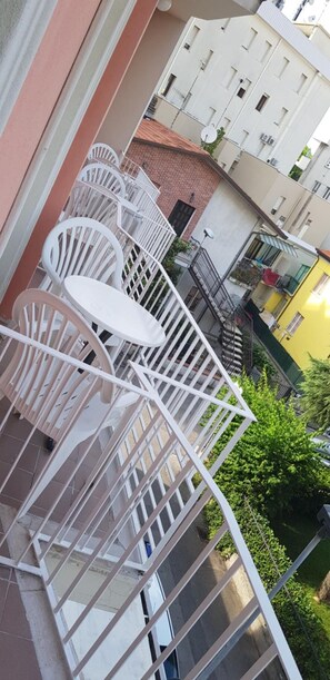 Uma varanda com cadeiras e mesas de metal branco, um muro de tijolos vermelhos e vista para edifícios vizinhos.