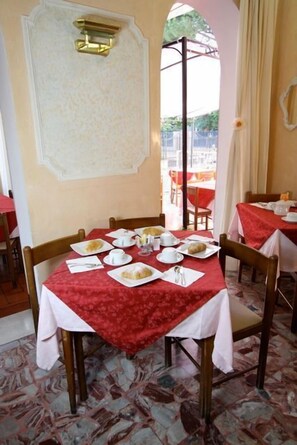 Uma sala de jantar com mesas preparadas para o café da manhã, com pratos de comida, xícaras e talheres.