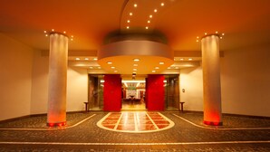 Um hall espaçoso com piso circular estampado no centro, colunas imponentes e teto com iluminação embutida.