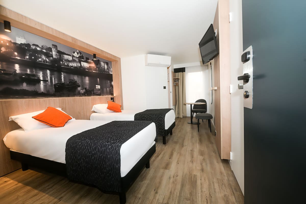 Quarto de hotel com duas camas, televisão, escrivaninha e um mural com vista para a cidade.