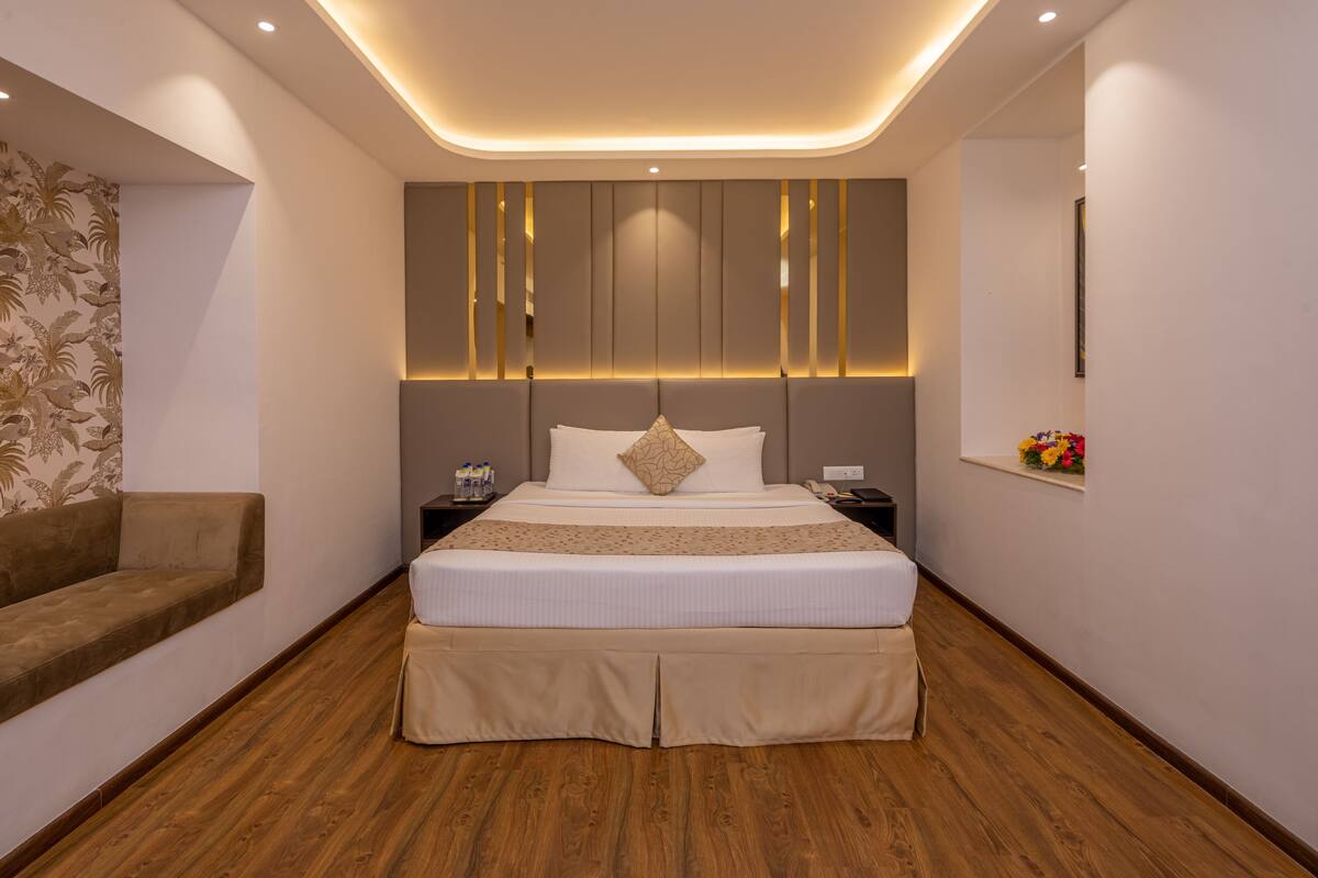 Quarto moderno com uma cama grande, mesas de cabeceira, um criado-mudo, um sofá e uma prateleira fixada na parede com flores.