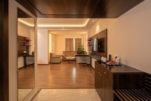 Quarto de hotel moderno com piso de madeira, um sofá, uma mesa de centro, uma TV e uma escrivaninha com cadeira.