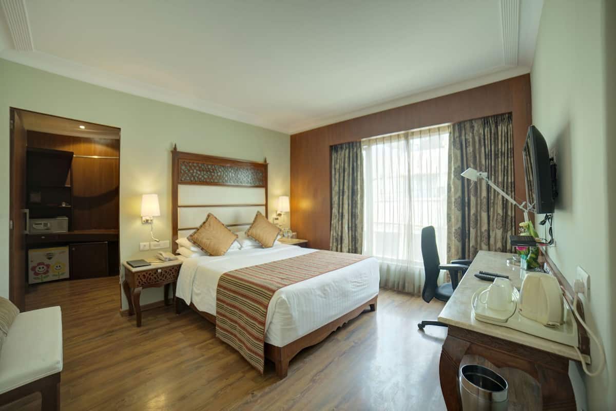 Quarto de hotel com cama, mesas de cabeceira, escrivaninha, cadeira, televisão e janela com cortinas.
