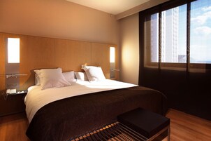 Quarto de hotel moderno com uma cama grande, mesas de cabeceira e uma janela com cortinas.