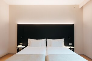 Uma cama de casal com cabeceira preta e duas mesas de cabeceira, cada uma com uma luminária e um telefone.