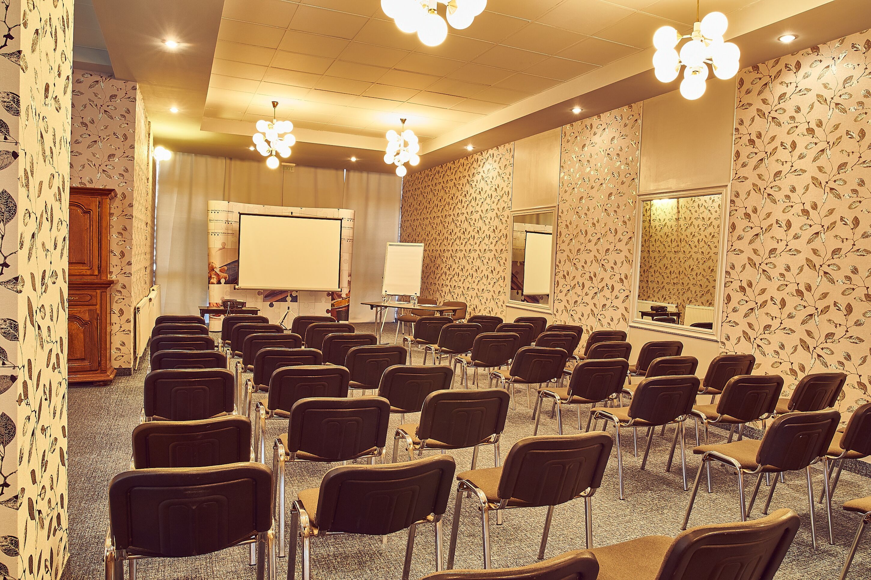 Uma sala de conferências com fileiras de cadeiras, um quadro branco e uma tela de projeção.
