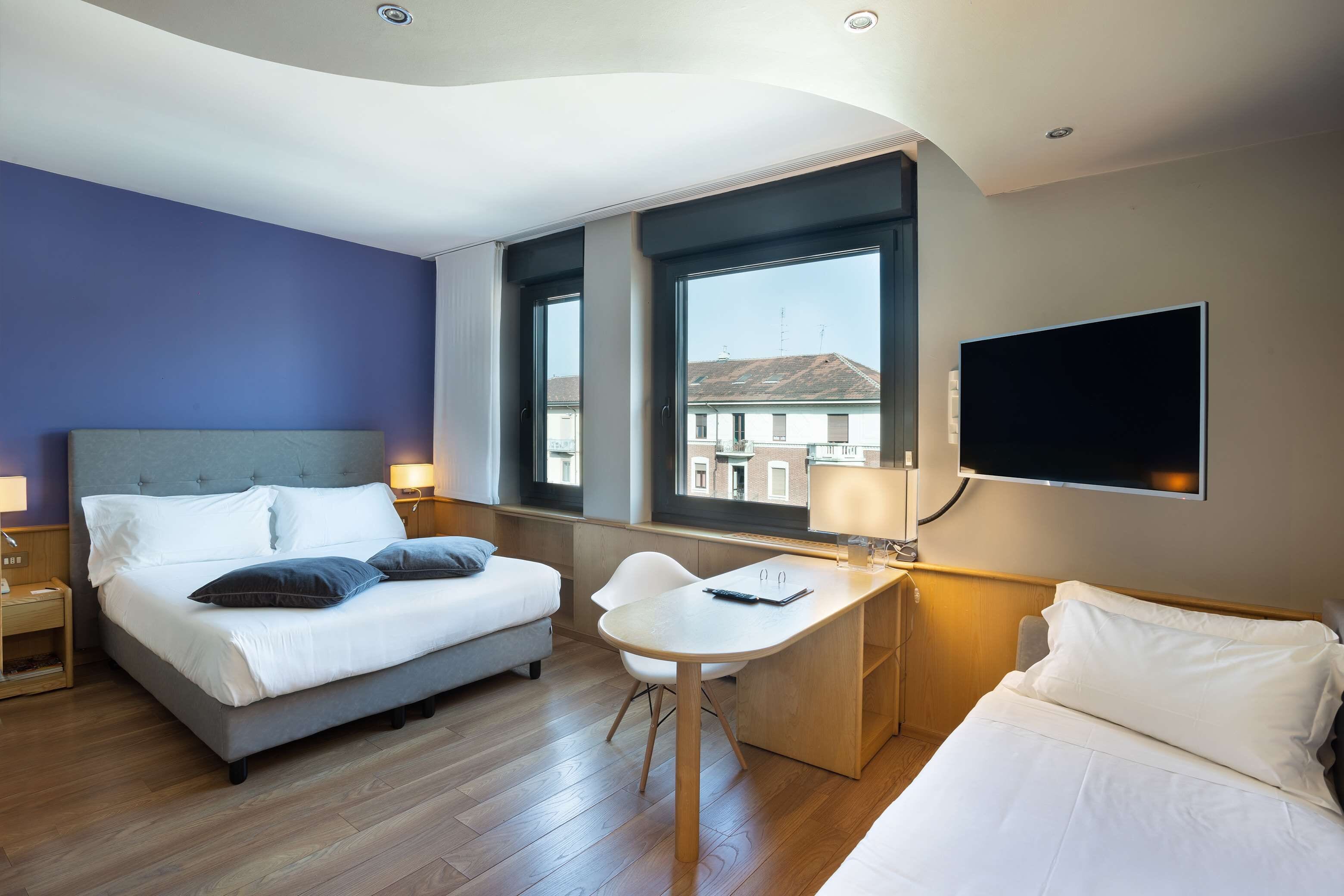 Quarto de hotel moderno com cama, escrivaninha e televisão.