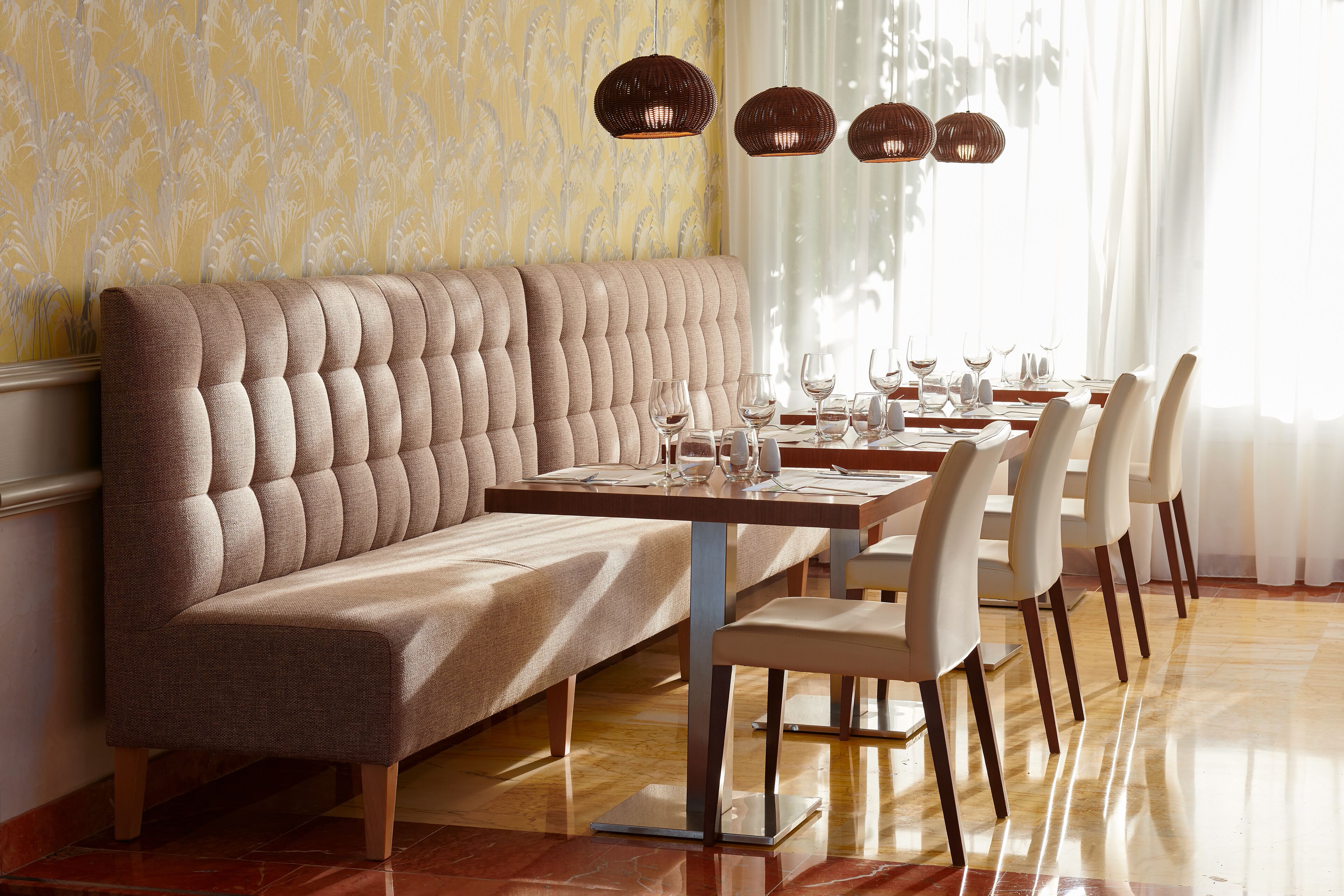 Uma sala de jantar com um sofá estofado, uma mesa retangular posta para seis pessoas e uma fileira de cadeiras.