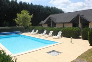 Piscina com espreguiçadeiras brancas e um edifício com telhado inclinado.