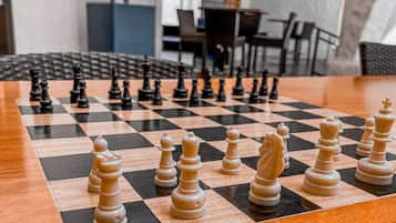 Um tabuleiro de xadrez com as peças dispostas para um jogo, uma mesa e cadeiras ao fundo.