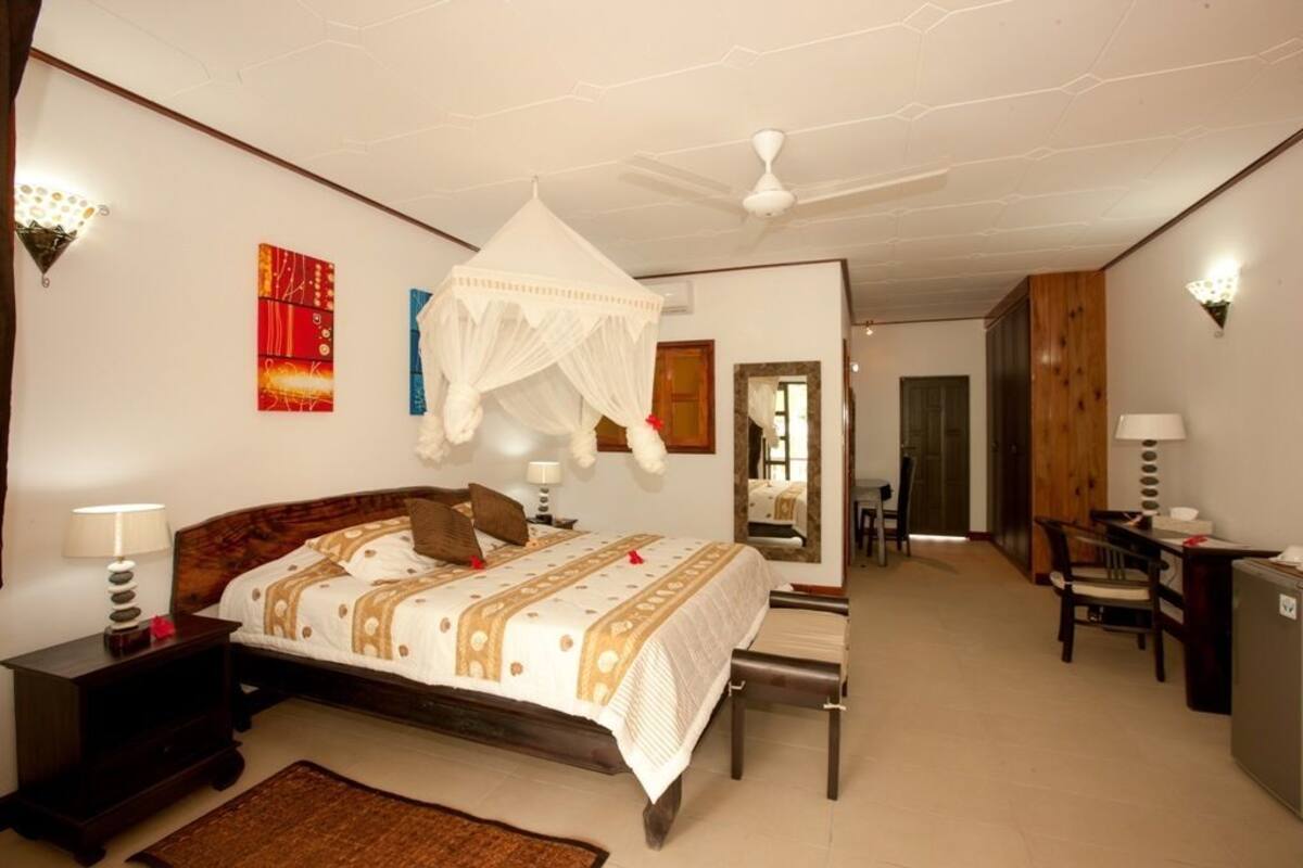 Quarto com cama, mesas de cabeceira, escrivaninha e uma cadeira.