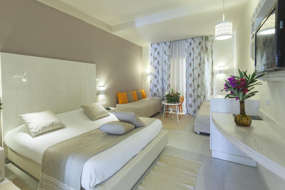 Quarto de hotel moderno com uma cama grande, um sofá pequeno, área de refeições e uma cozinha compacta.