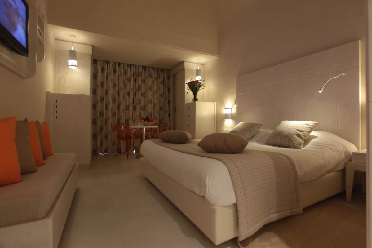 Quarto de hotel moderno com uma cama grande, um sofá, uma mesa de jantar e uma televisão.