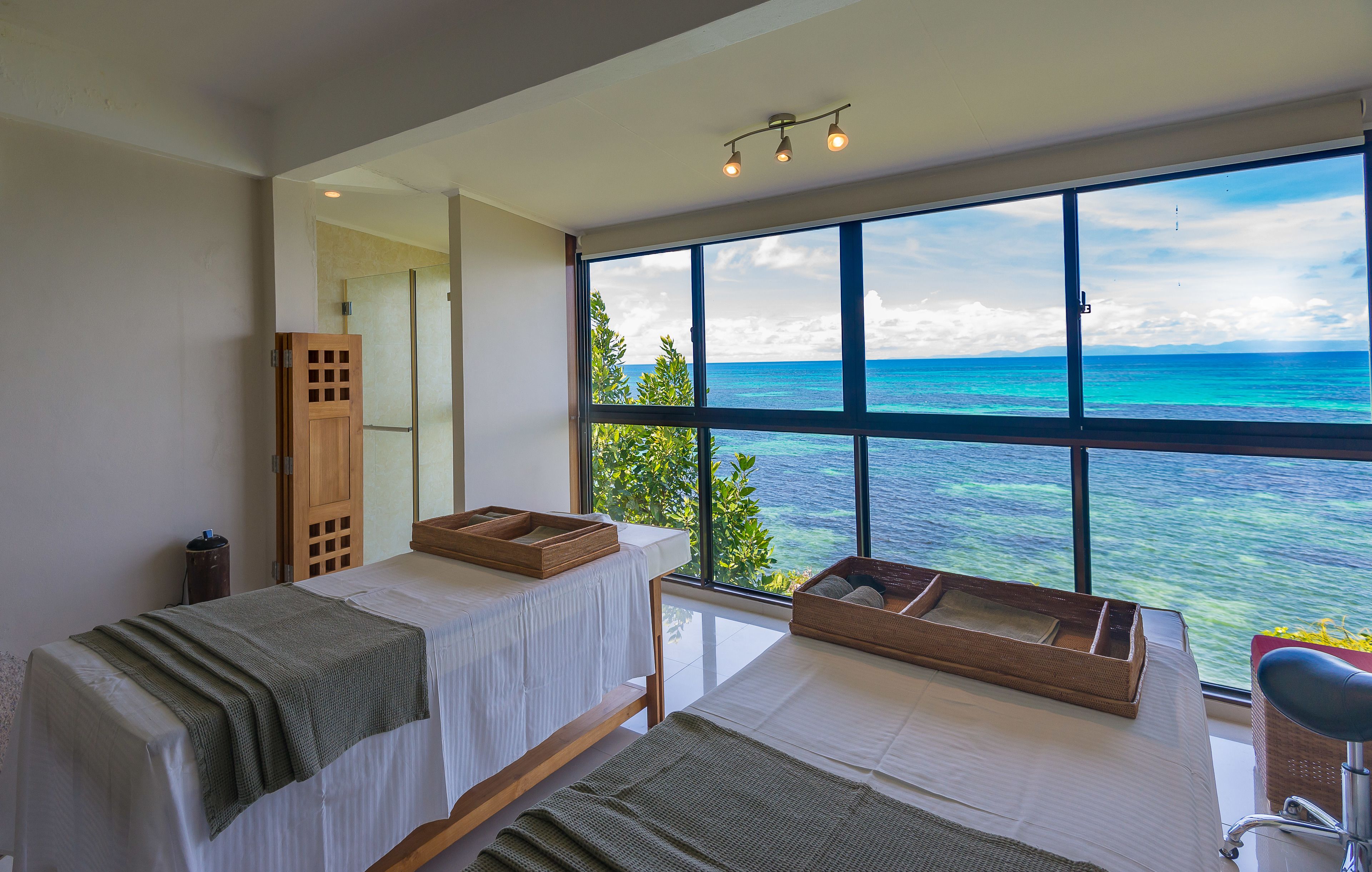 Quarto moderno com duas camas, janelas amplas e vista para o mar.