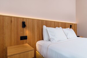 Quarto de hotel com cabeceira de madeira, mesa de cabeceira e cama com roupa de cama branca.