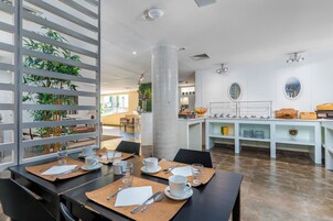 Uma sala de jantar moderna com mesas preparadas para o pequeno-almoço, um buffet com diversas opções de comida e vista para a rua.