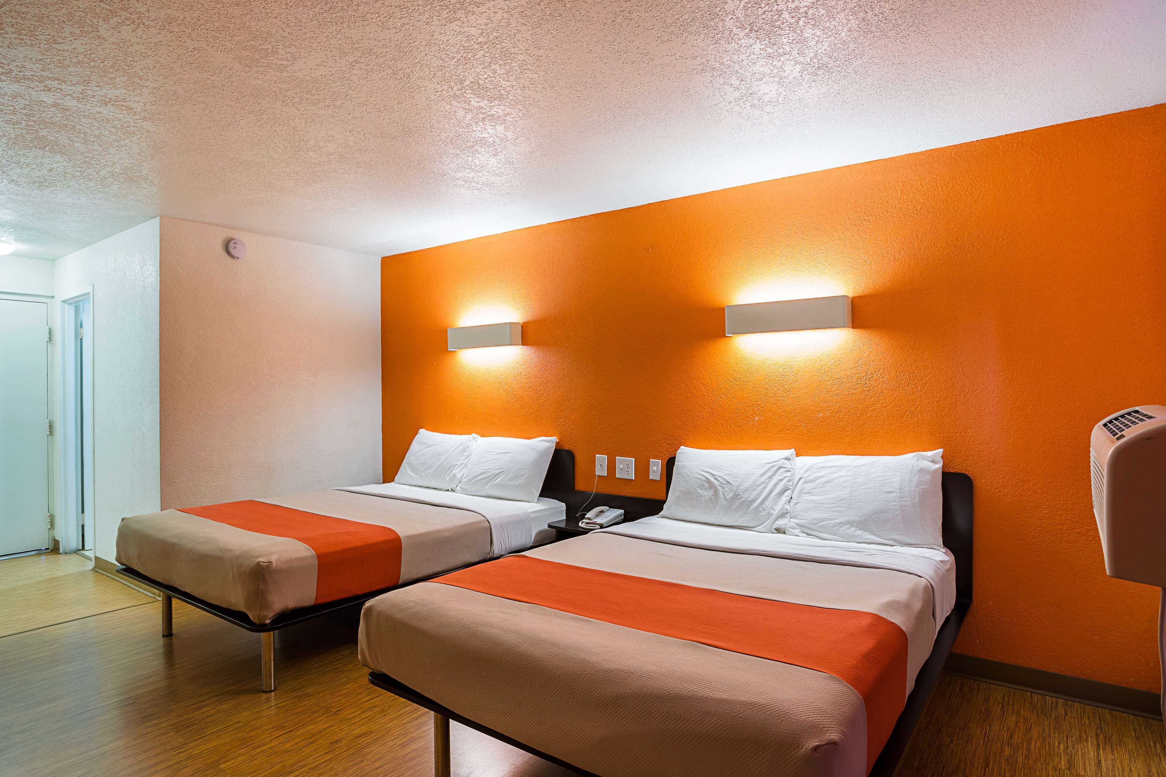 Quarto de hotel com duas camas, piso de madeira e parede em tons de laranja.