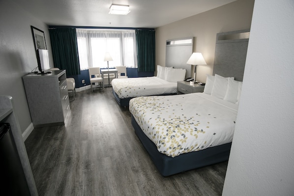 Quarto de hotel com duas camas, uma escrivaninha, uma cadeira, abajur, telefone e televisão.