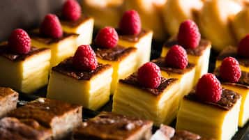 Diversos doces quadrados com cobertura dourada, alguns adornados com framboesas.