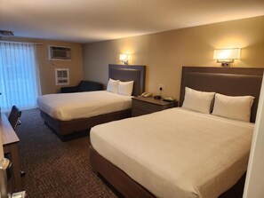 Quarto de hotel com duas camas, uma escrivaninha e uma cadeira.