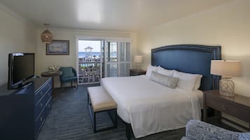 Quarto de hotel com cama, escrivaninha, cadeira, televisão e varanda vista para o oceano.