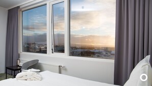 Quarto de hotel com uma janela grande, uma cama, uma cadeira e uma mesa.