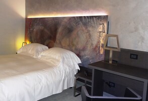 Quarto de hotel moderno com uma cama grande, uma mesa de escritório e uma obra de arte abstrata original na parede.