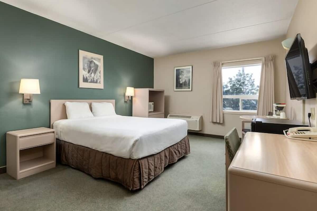 Quarto de hotel com cama, mesas de cabeceira, escrivaninha, cadeira, televisão e janela com cortinas.