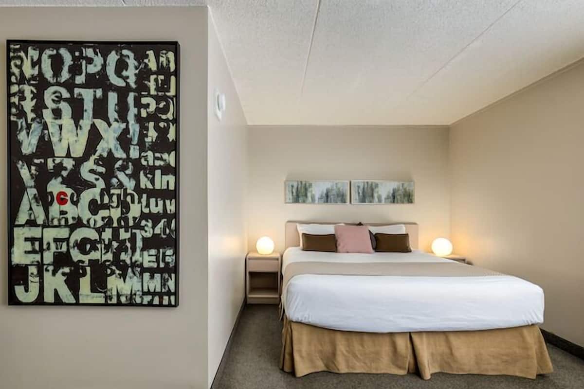 Quarto com uma cama, duas mesas de cabeceira e uma obra de arte na parede.