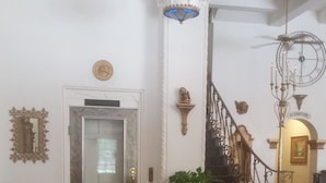 Um saguão com piso estampado, escada, lustre e porta com painel de vidro.