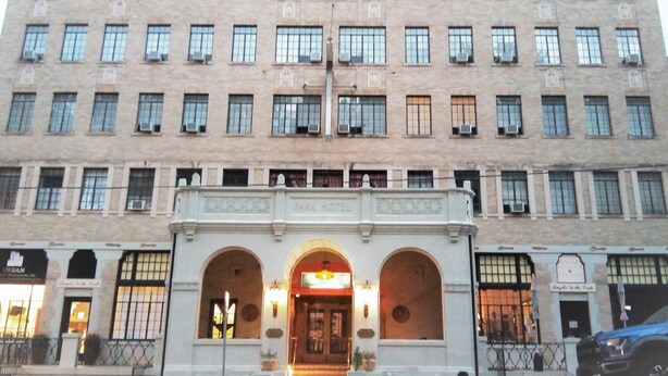 Um edifício de vários andares com uma entrada central destacada por um arco decorativo e uma placa que diz 