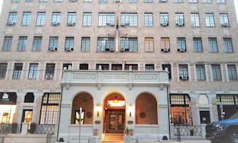 Um edifício de vários andares com uma entrada central destacada por um arco decorativo e uma placa que diz