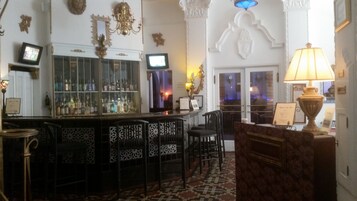 Uma área de bar com balcão, banquetas e uma tela de televisão. Há elementos decorativos nas paredes e um piso estampado.