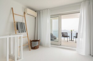 Quarto moderno com corrimão branco, escada de madeira, cesto de vime e vista para o mar através de uma porta de vidro.