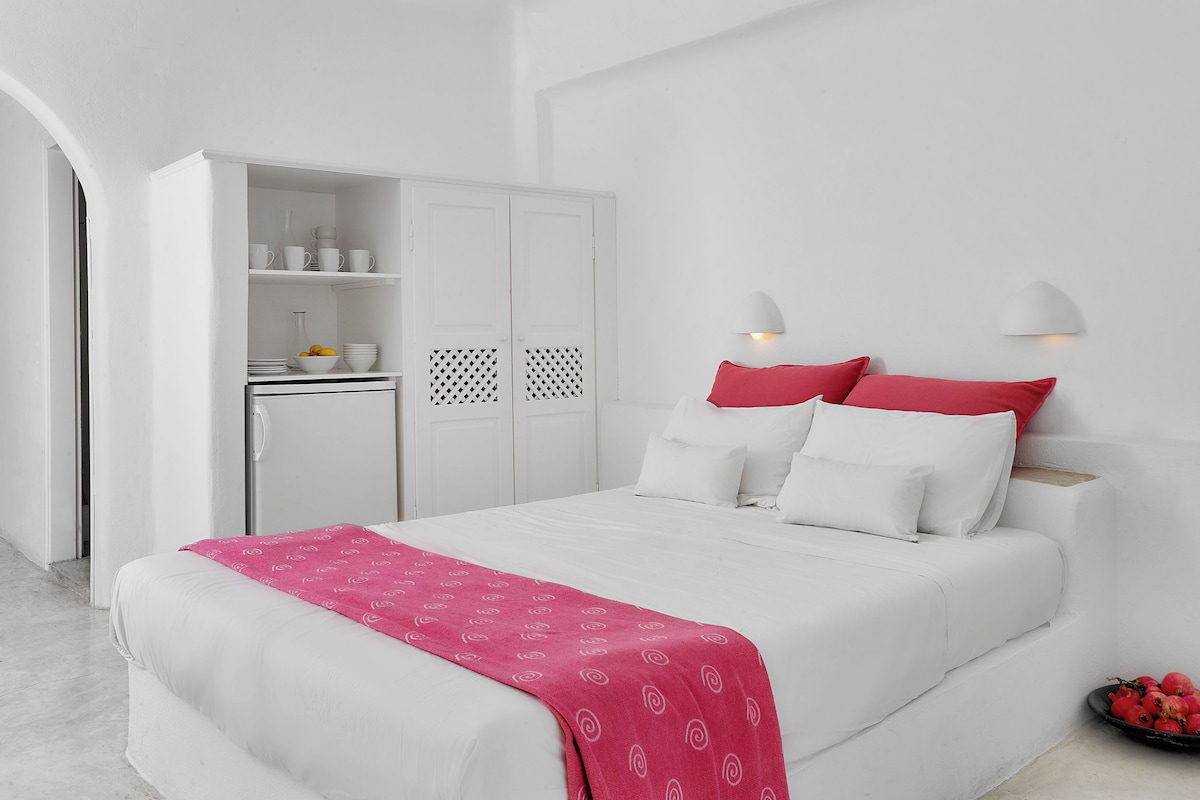 Quarto branco com uma cama, um guarda-roupa e uma pequena cozinha.