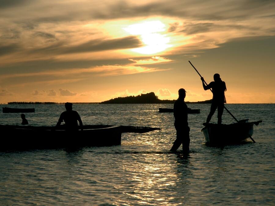 Um pôr do sol sobre águas calmas, com vários barcos e pessoas.