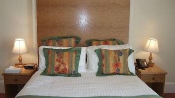 Cama bem arrumada com almofadas de padrão floral e colcha combinando, acompanhada por mesas de cabeceira com abajures e um telefone.