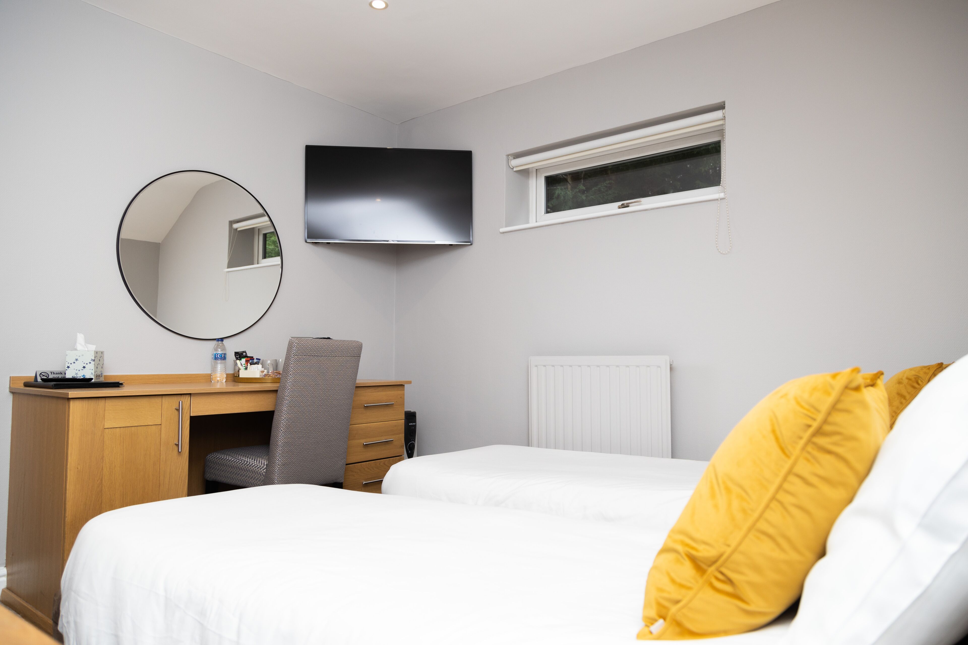 Quarto de hotel com uma cama, uma mesa com cadeira, televisão fixada na parede e janela com cortina.