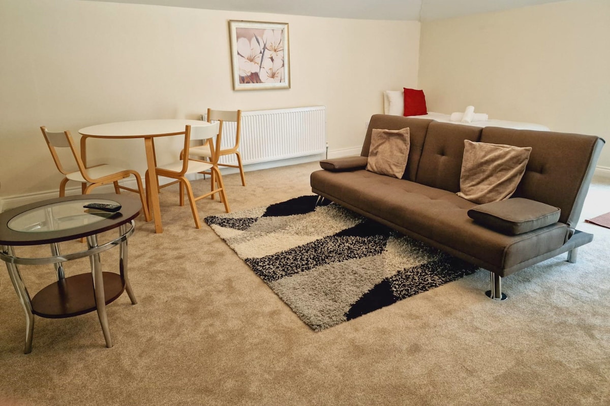Uma sala de estar com um sofá marrom, duas cadeiras, uma mesa de vidro pequena e um tapete preto e branco.