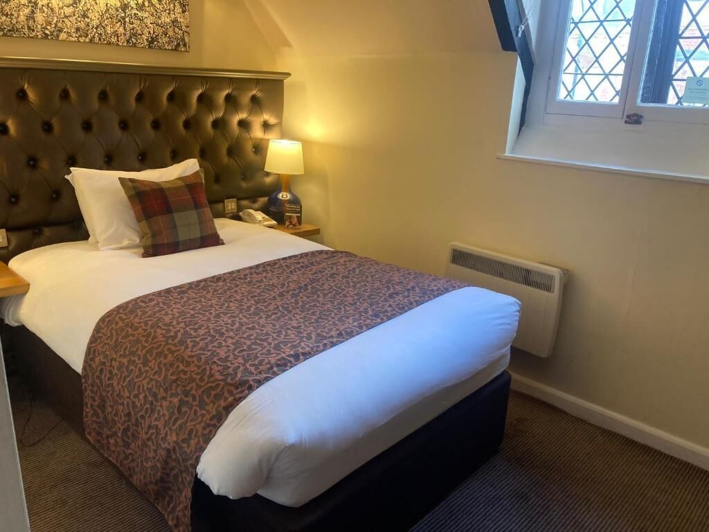 Quarto de hotel com cabeceira estofada, cama com colcha estampada, luminária de cabeceira e janela com vista.