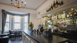 Espaço de bar com diversas garrafas de bebidas, uma máquina de café e opções de assentos.