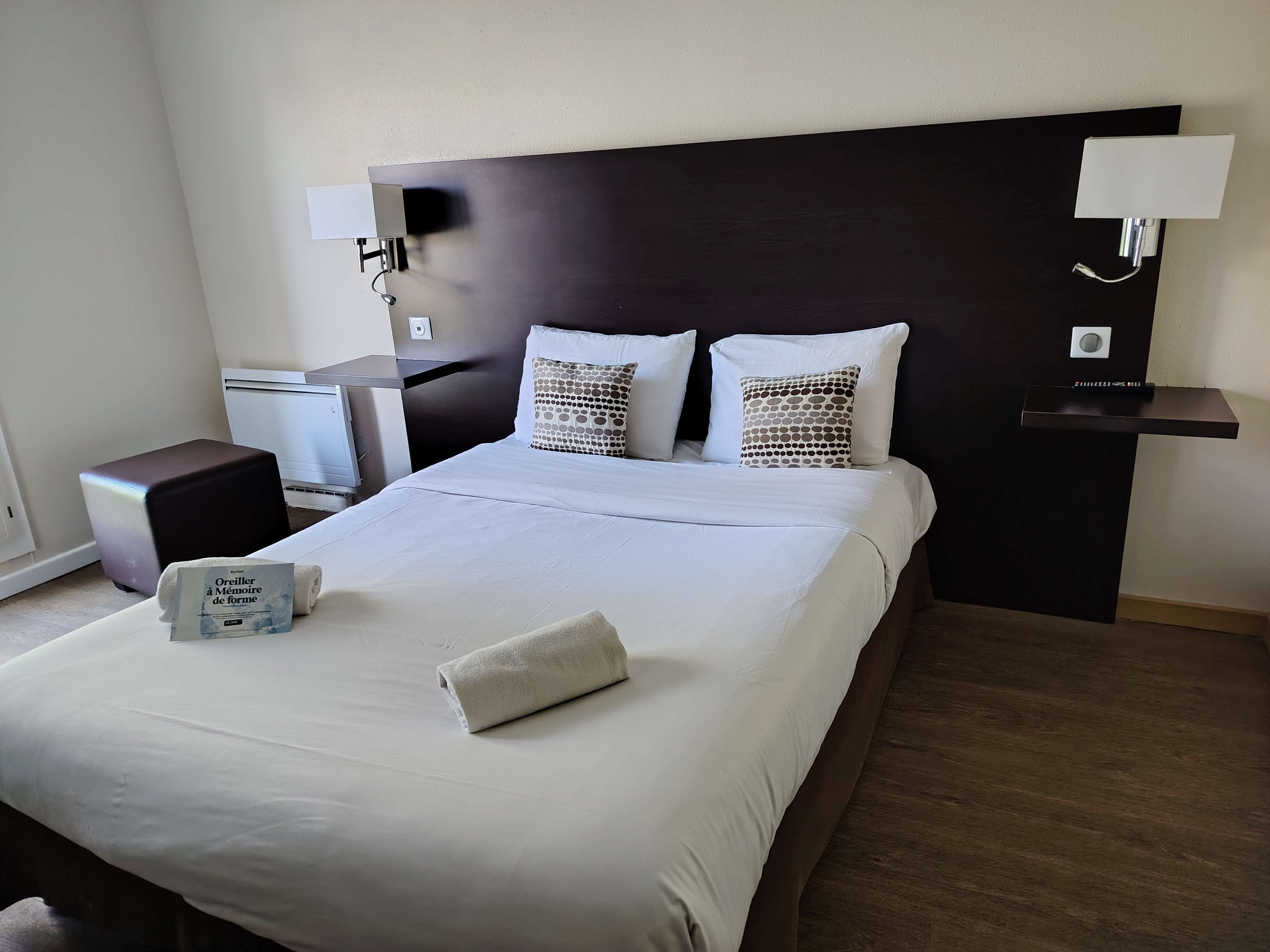Quarto de hotel com uma cama grande, duas mesas de cabeceira, uma escrivaninha e uma cadeira.